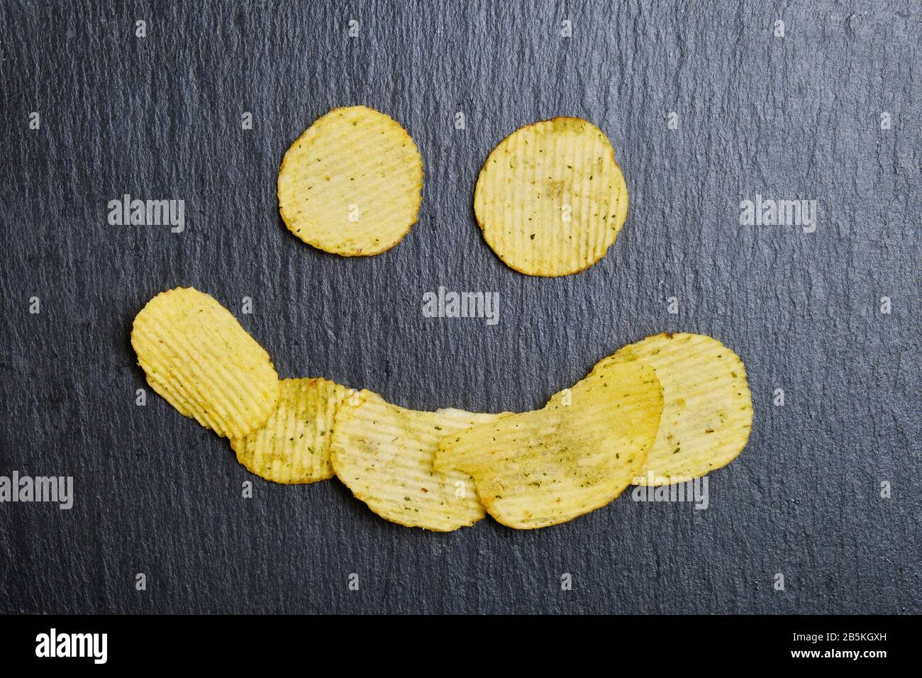 Corrugated chips on a black stone utensil. Abstract smiley. Top view ...