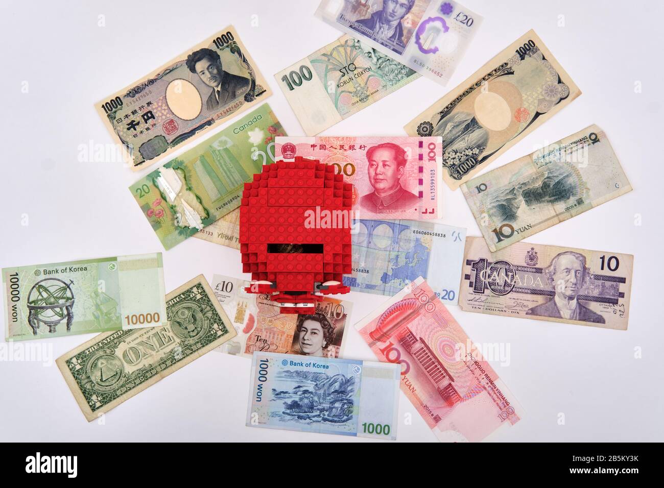 Assembled red lego piggy bank surrounded by different currencies paper ...