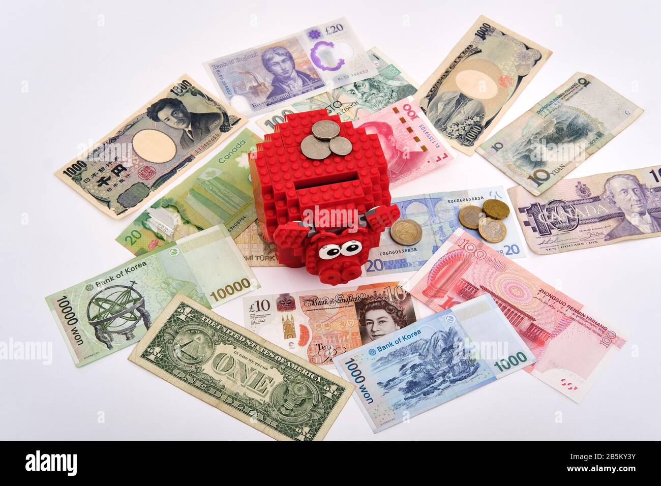 Assembled red lego piggy bank surrounded by different currencies paper ...