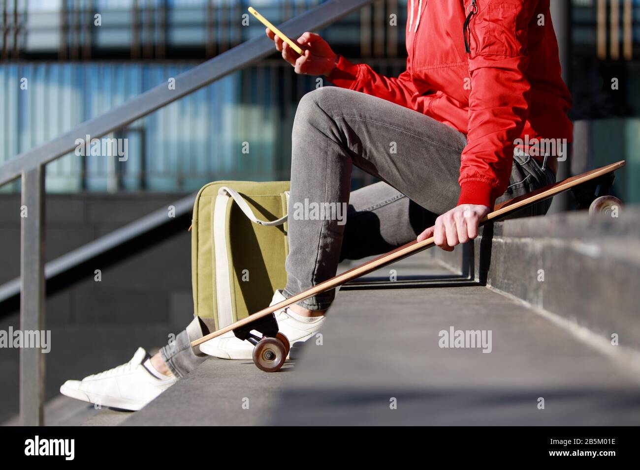 Stylish man longboarder in casual clothes using his smartphone, resting ...