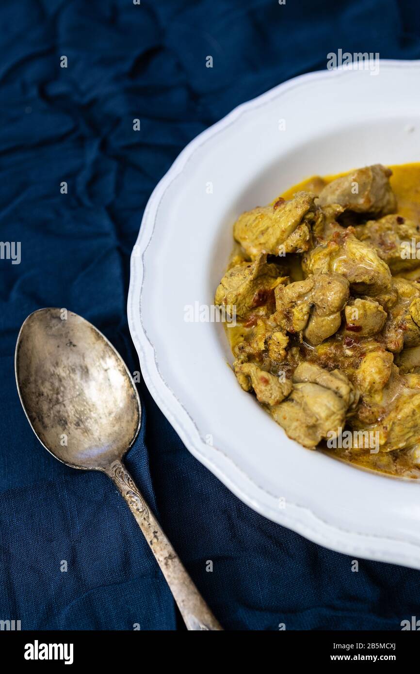 Orange spicy chicken curry in a white plate on a dark blue background ...