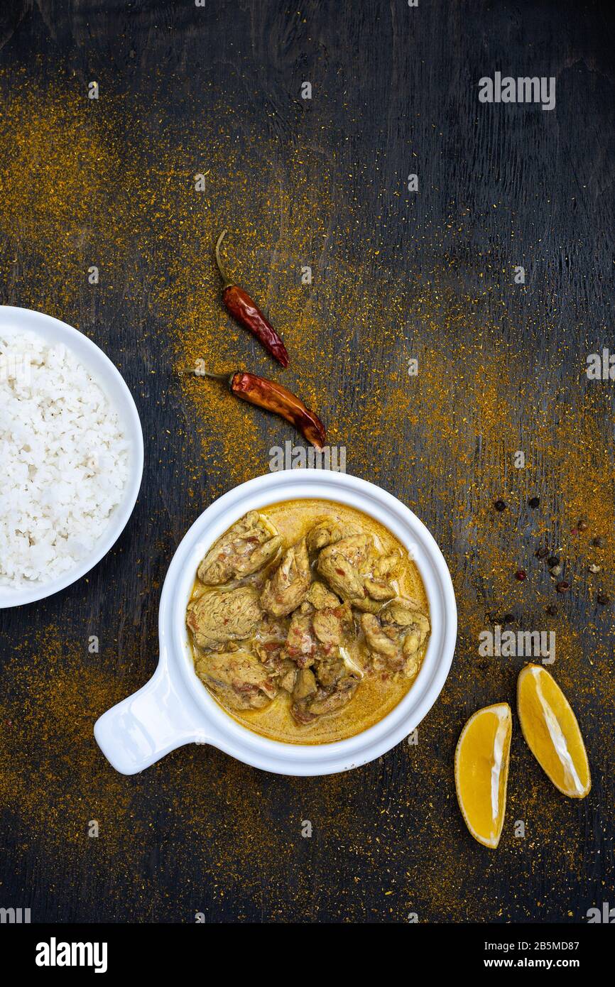 Orange spicy chicken curry and rice in simple white plates on a dark ...