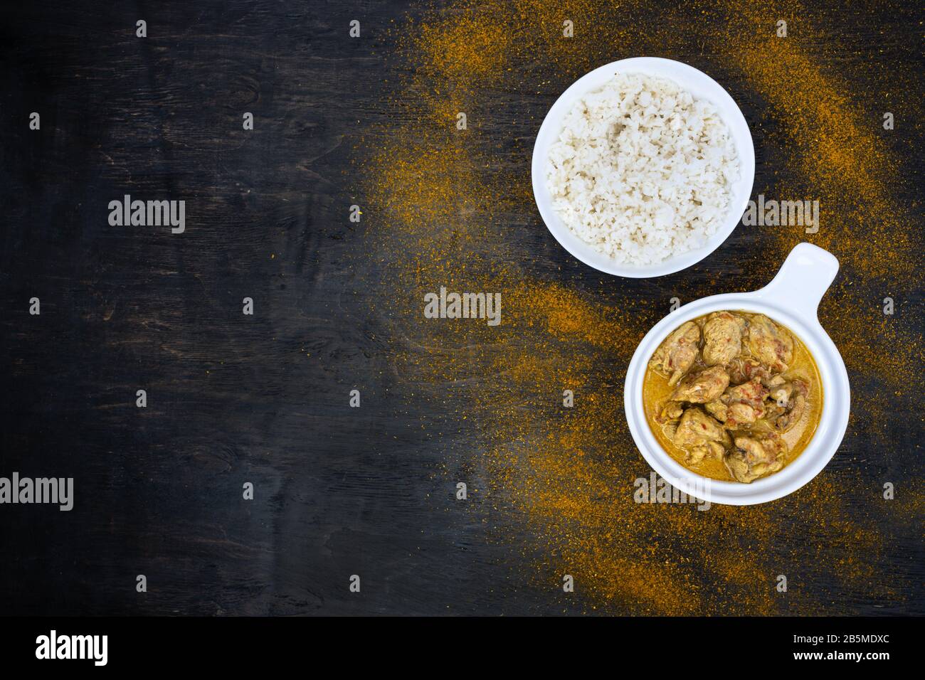 Orange spicy chicken curry and rice in simple white plates on a dark ...