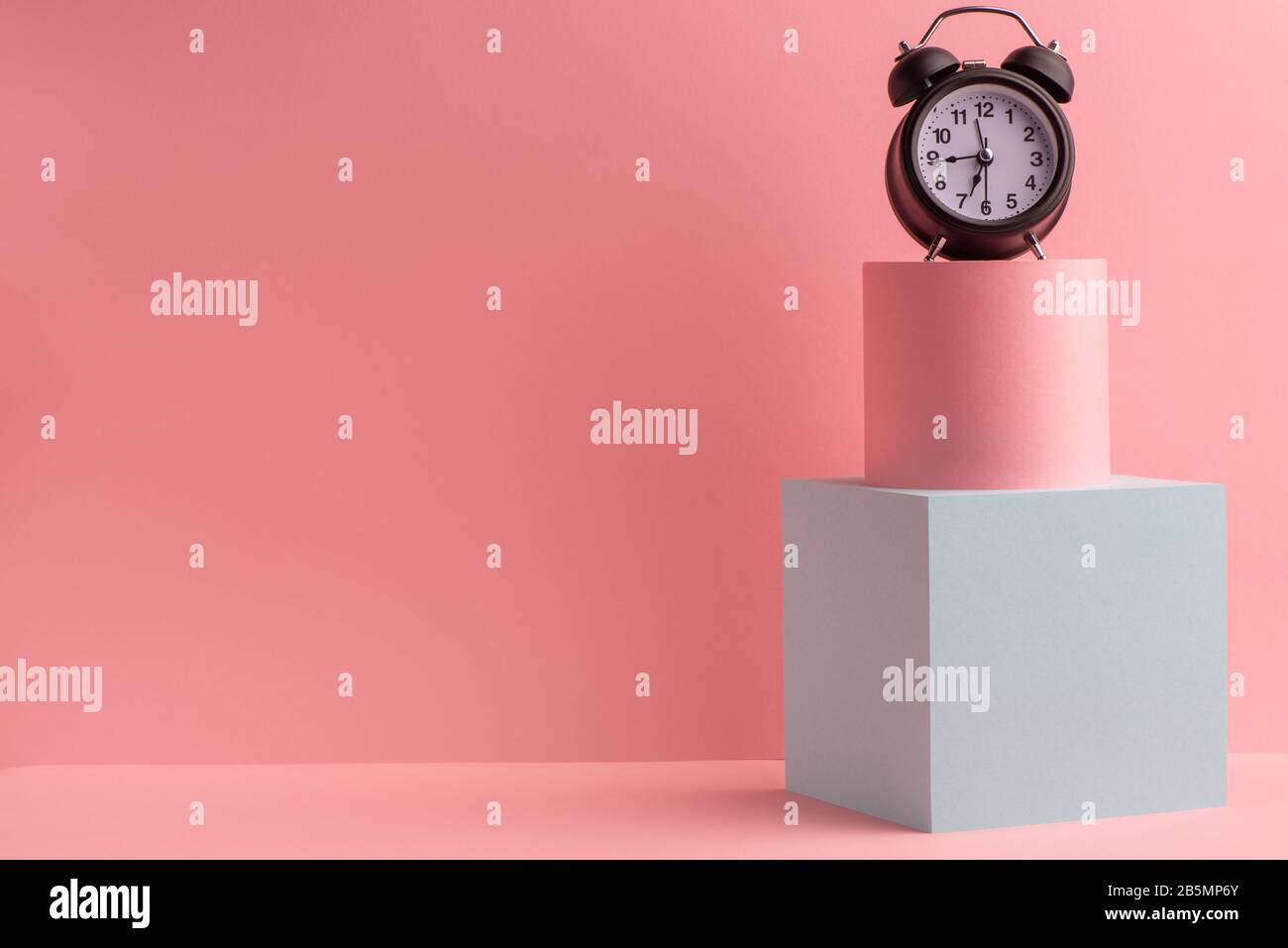 Vintage alarm clock on cube and cylinder on pink background Stock Photo ...