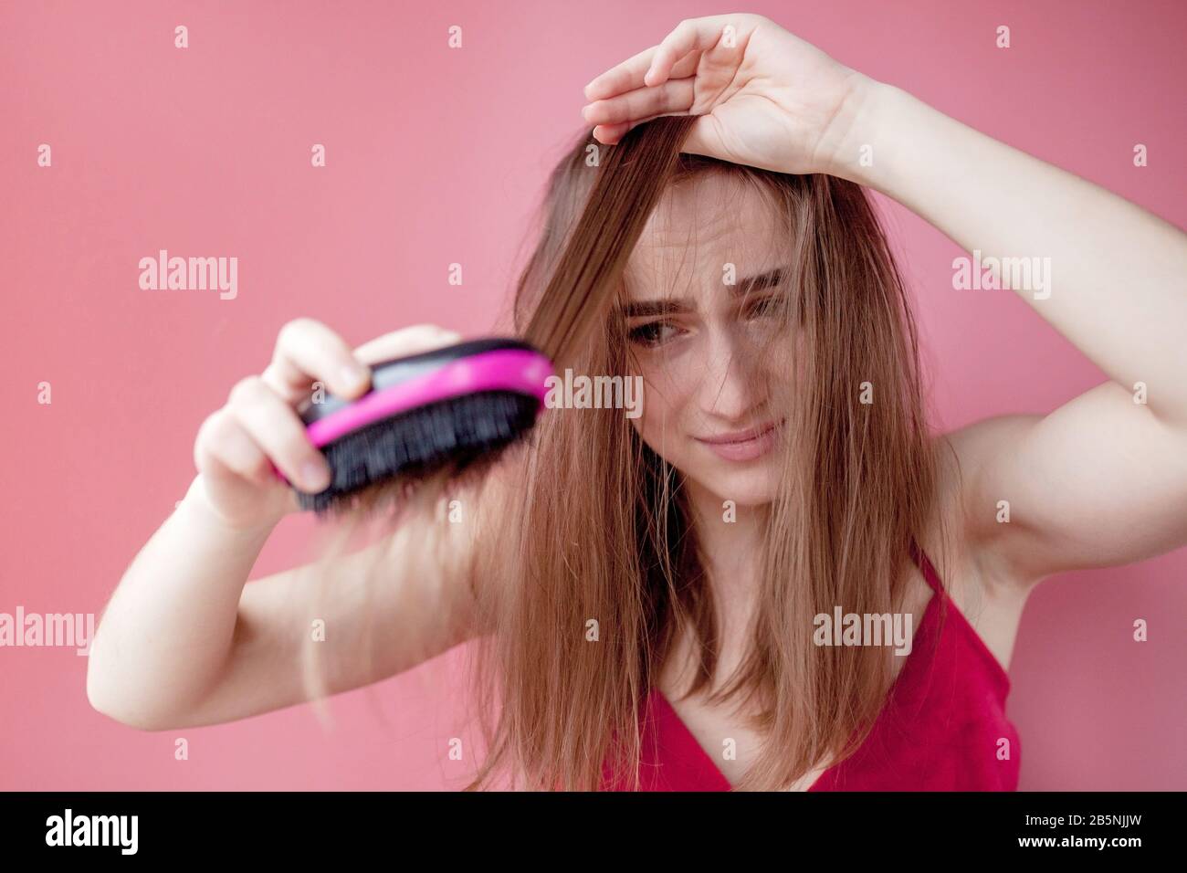 Young beautiful girl having problems while hair on pink background ...