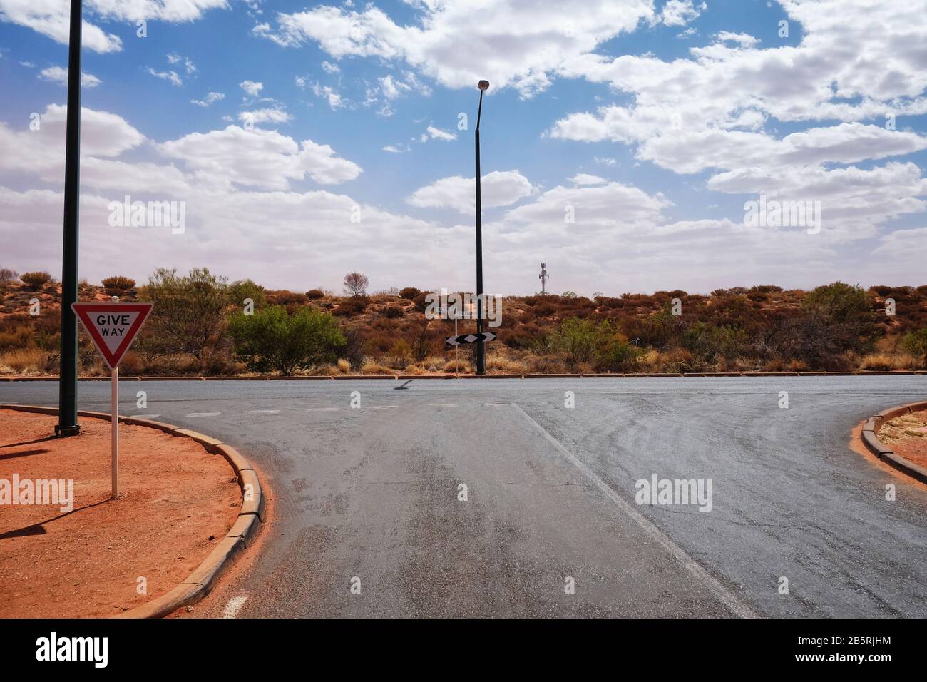 Poles signs and a black bitumen outback road, with scrub and red sandy ...