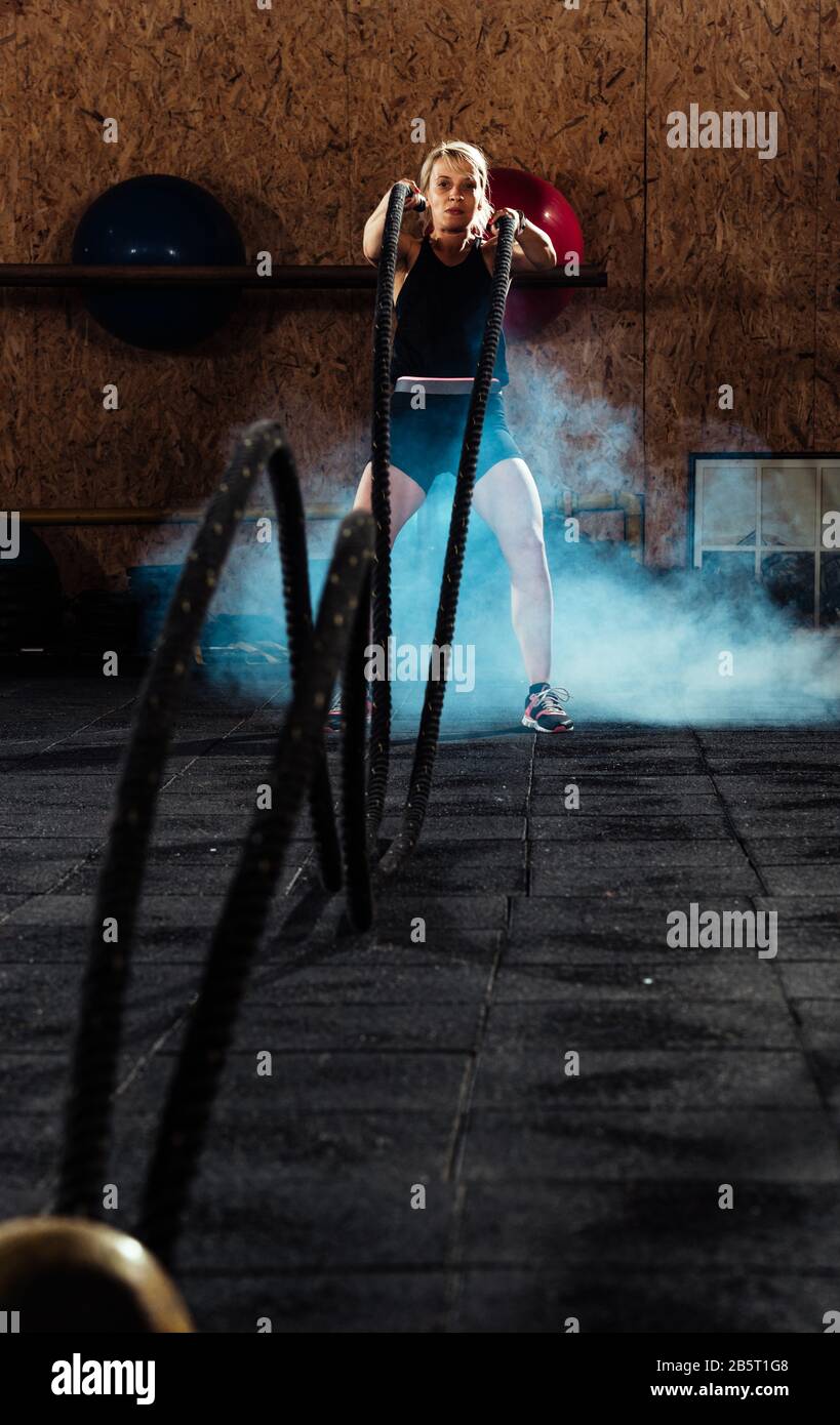 Athletic girl doing some cross-training exercises with a rope in gym ...