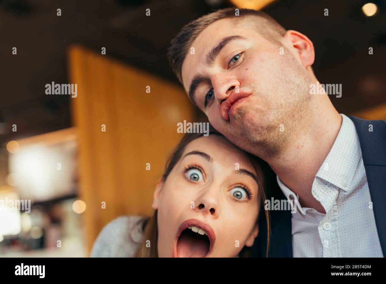 Couple having fun in a cafe ( coffee shop) while making crazy faces and ...
