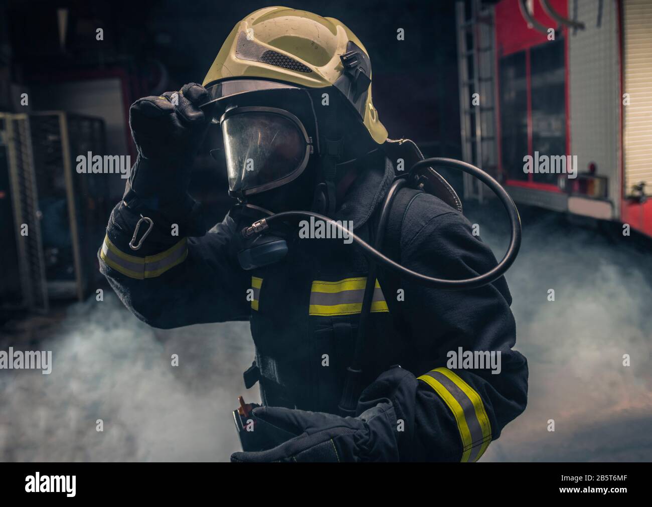 Portrait of a fireman wearing firefighter turnouts and helmet. Dark ...