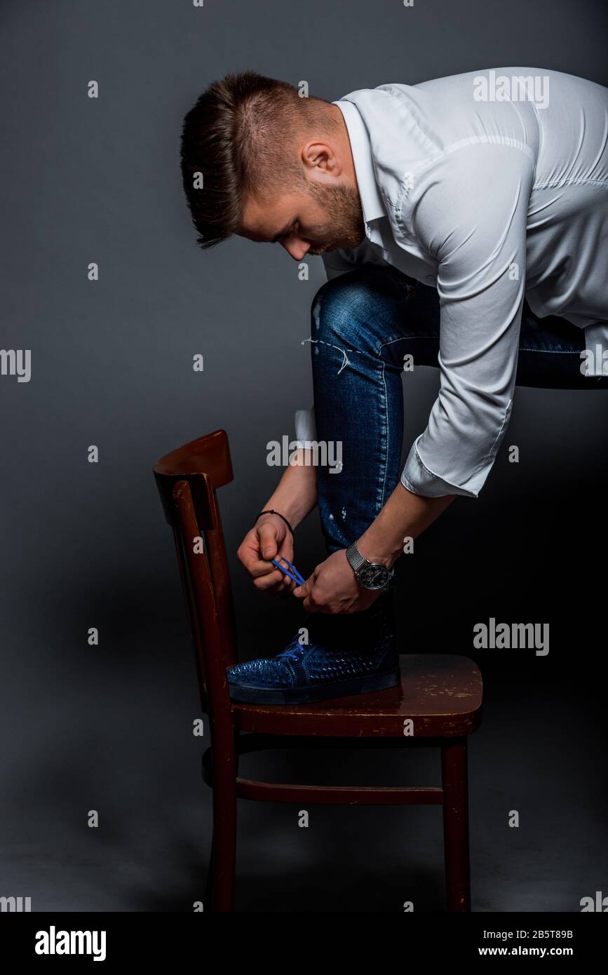 Cool young man dressed in white shirt tying shoe laces on cheir Stock ...