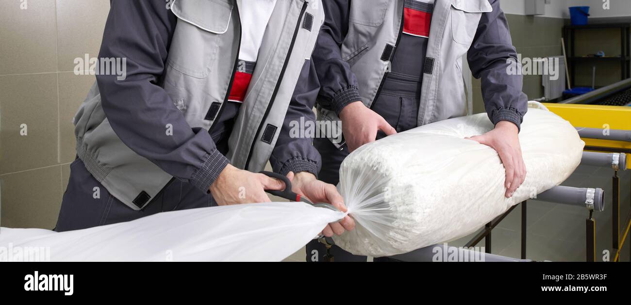 Men workers packing carpet in a plastic bag after cleaning it in ...