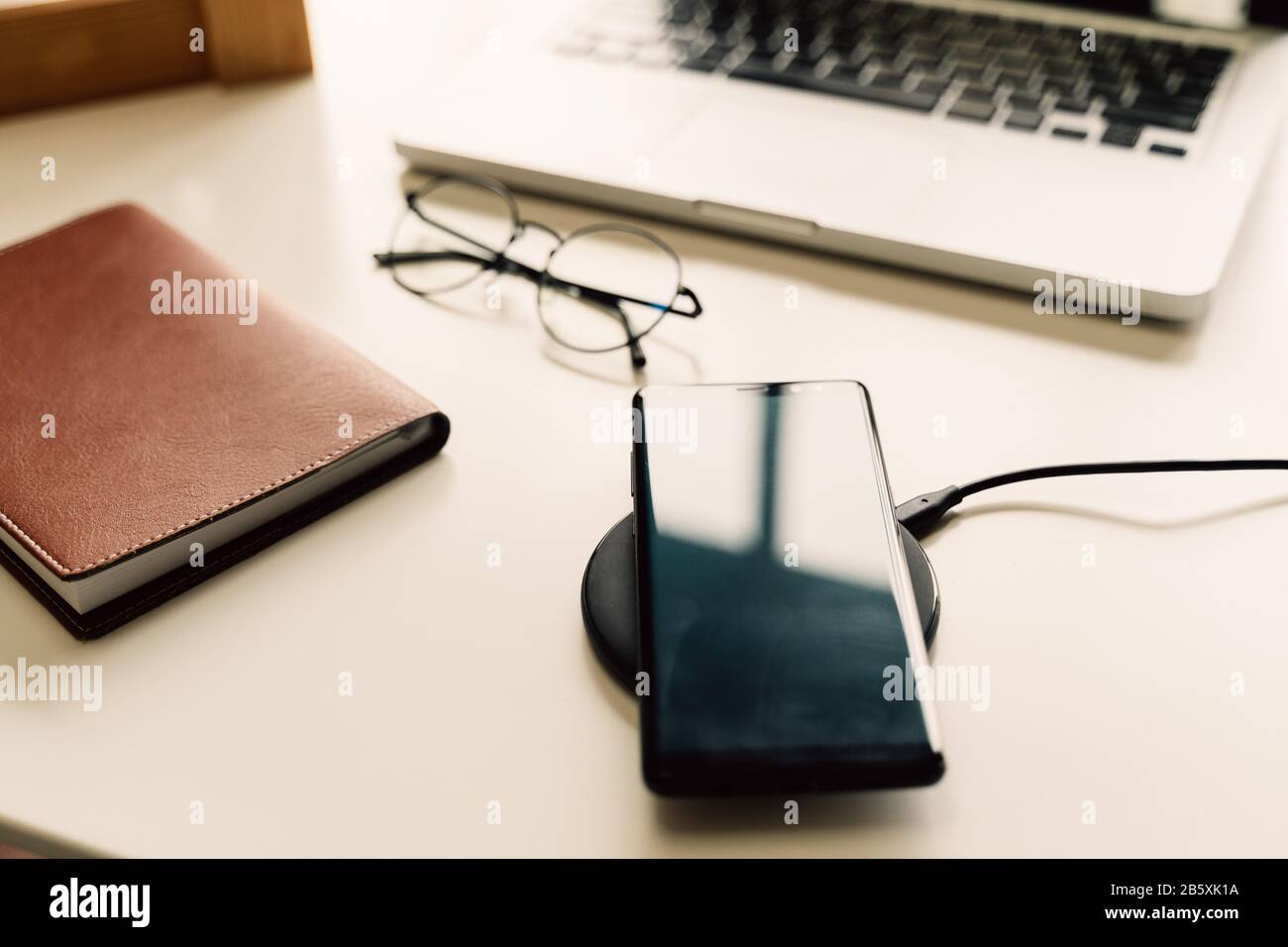 Smart phone being charged on wireless charger alongside with laptop ...