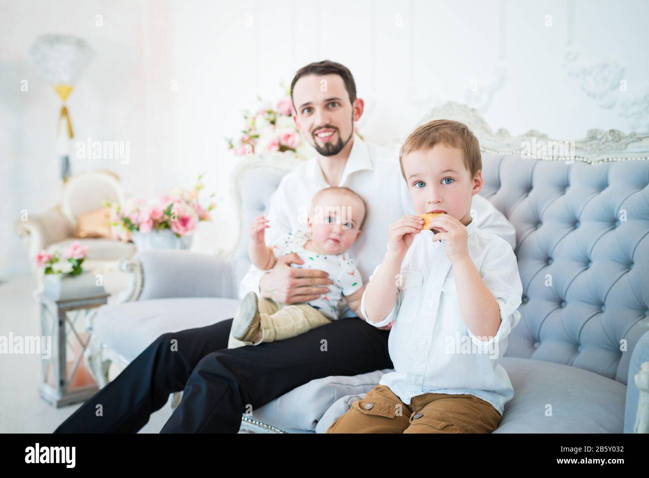 Positive young father is sitting on the blue couch with his little sons ...