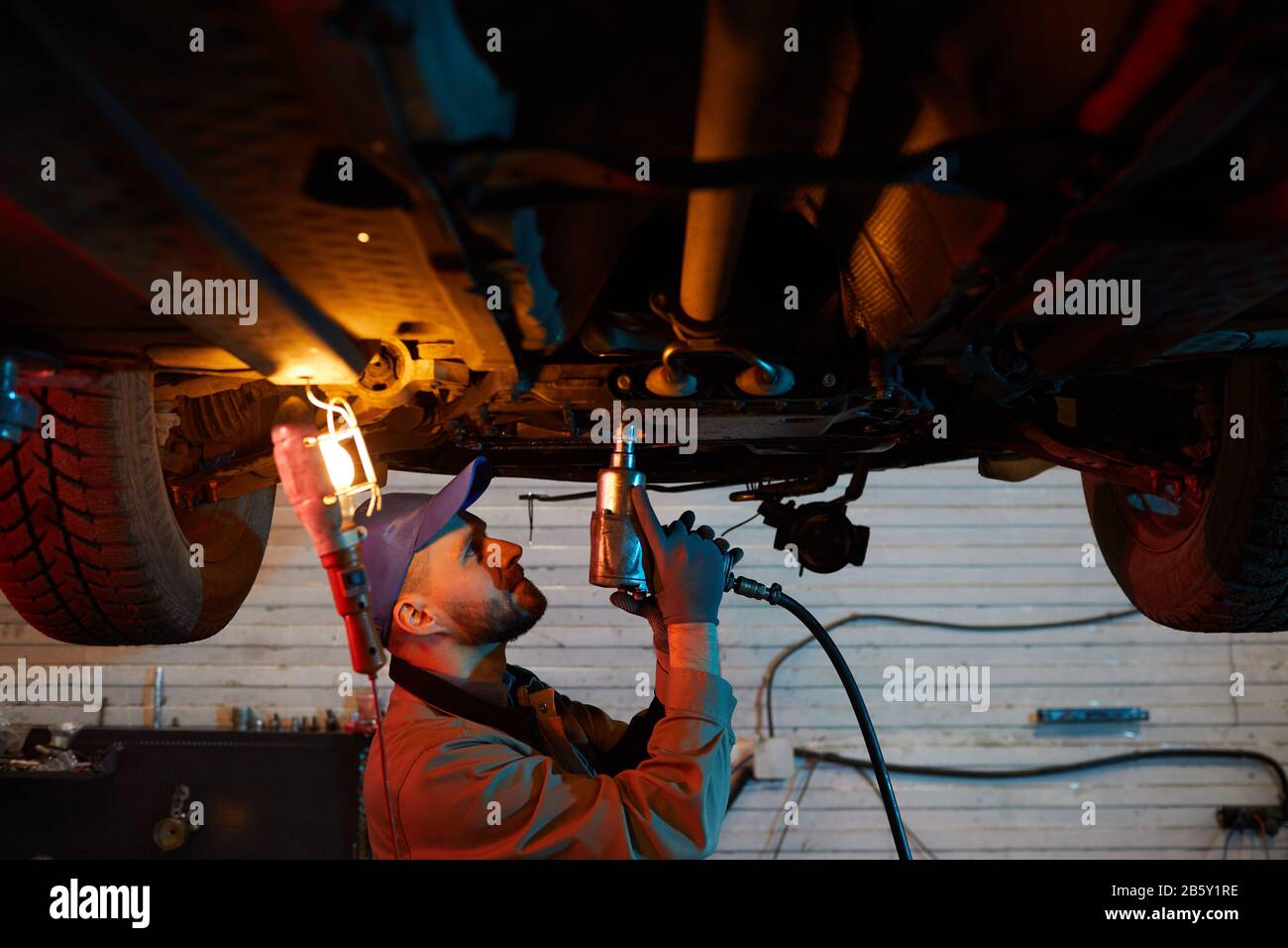 Professional auto mechanic standing under car fixing its parts ...