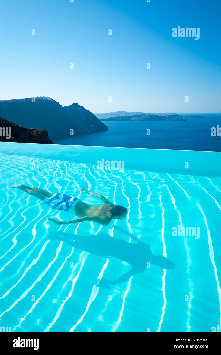Unrecognizable man swimming underwater in turquoise infinity pool ...