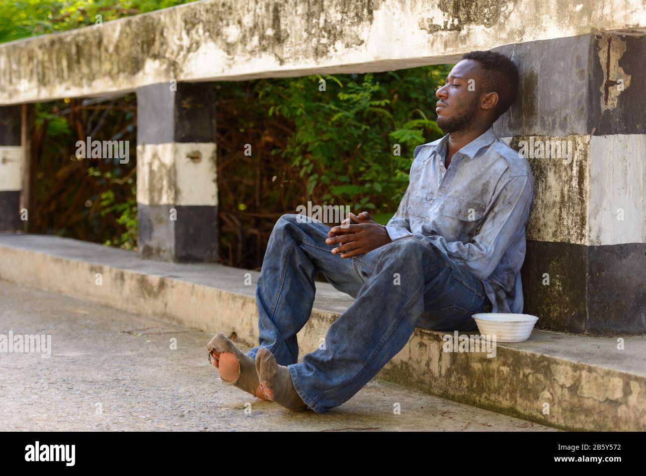 Young homeless African man with plastic bowl looking hungry Stock Photo ...
