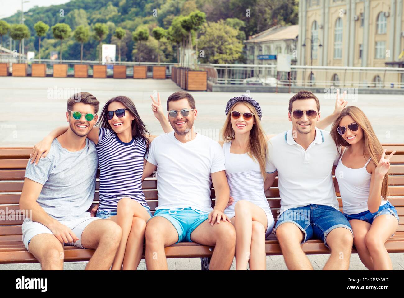 Cheerful happy best friends spending time together and sitting on bench ...