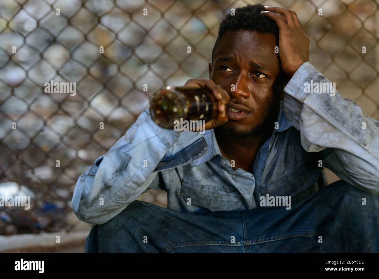 Depressed young homeless African man drinking beer Stock Photo - Alamy