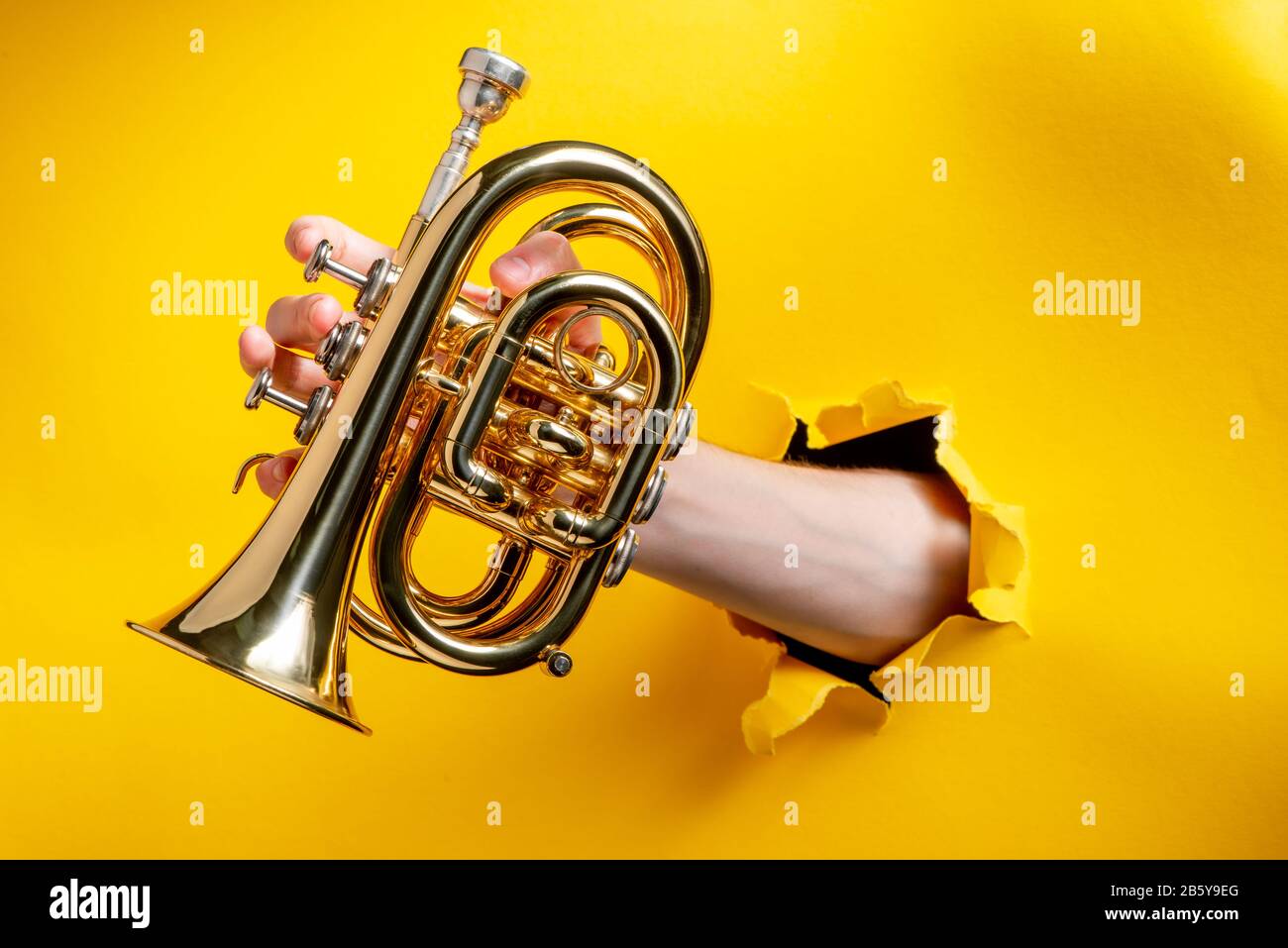 Hand playing a pocket trumpet through torn yellow paper background ...