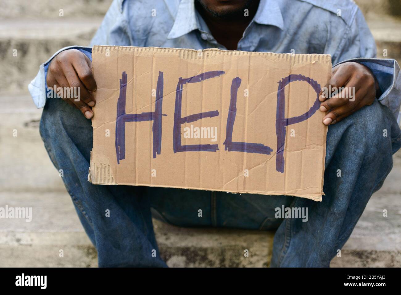 Hands of young homeless African man with cardboard sign asking for help ...