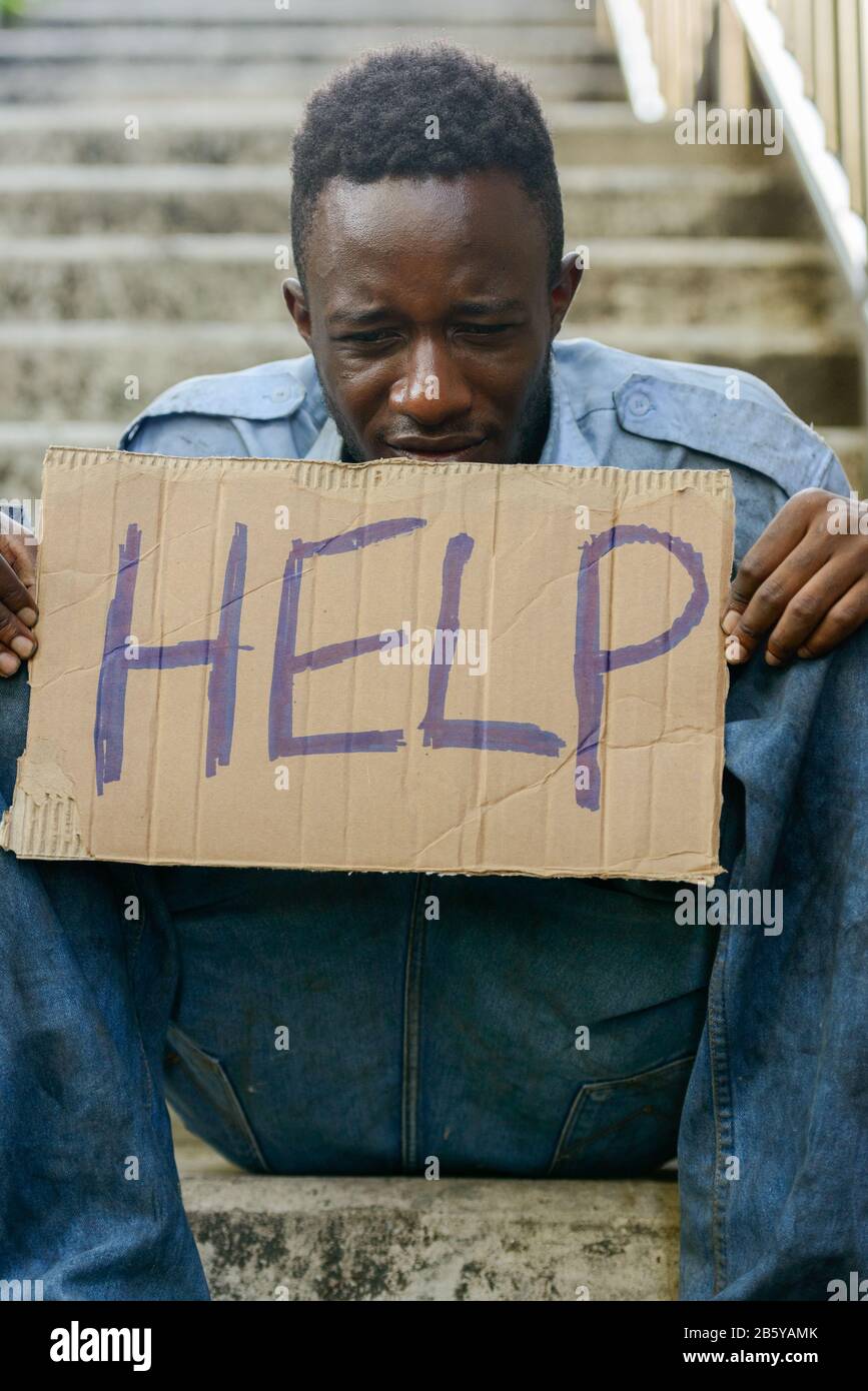Depressed young homeless African man with cardboard sign asking for ...