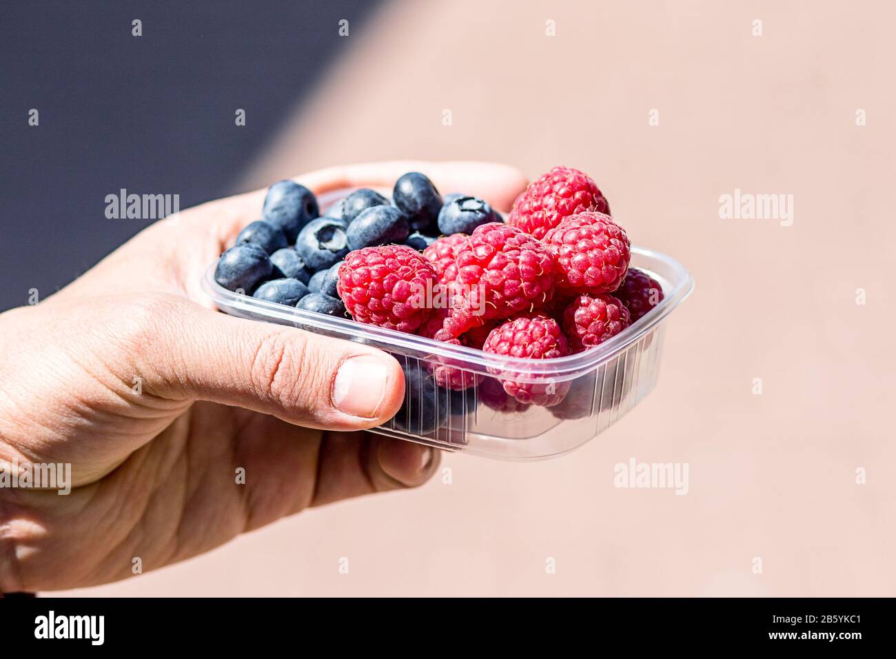 the guy is holding a tray of raspberries and blueberries. Vitamin-rich ...