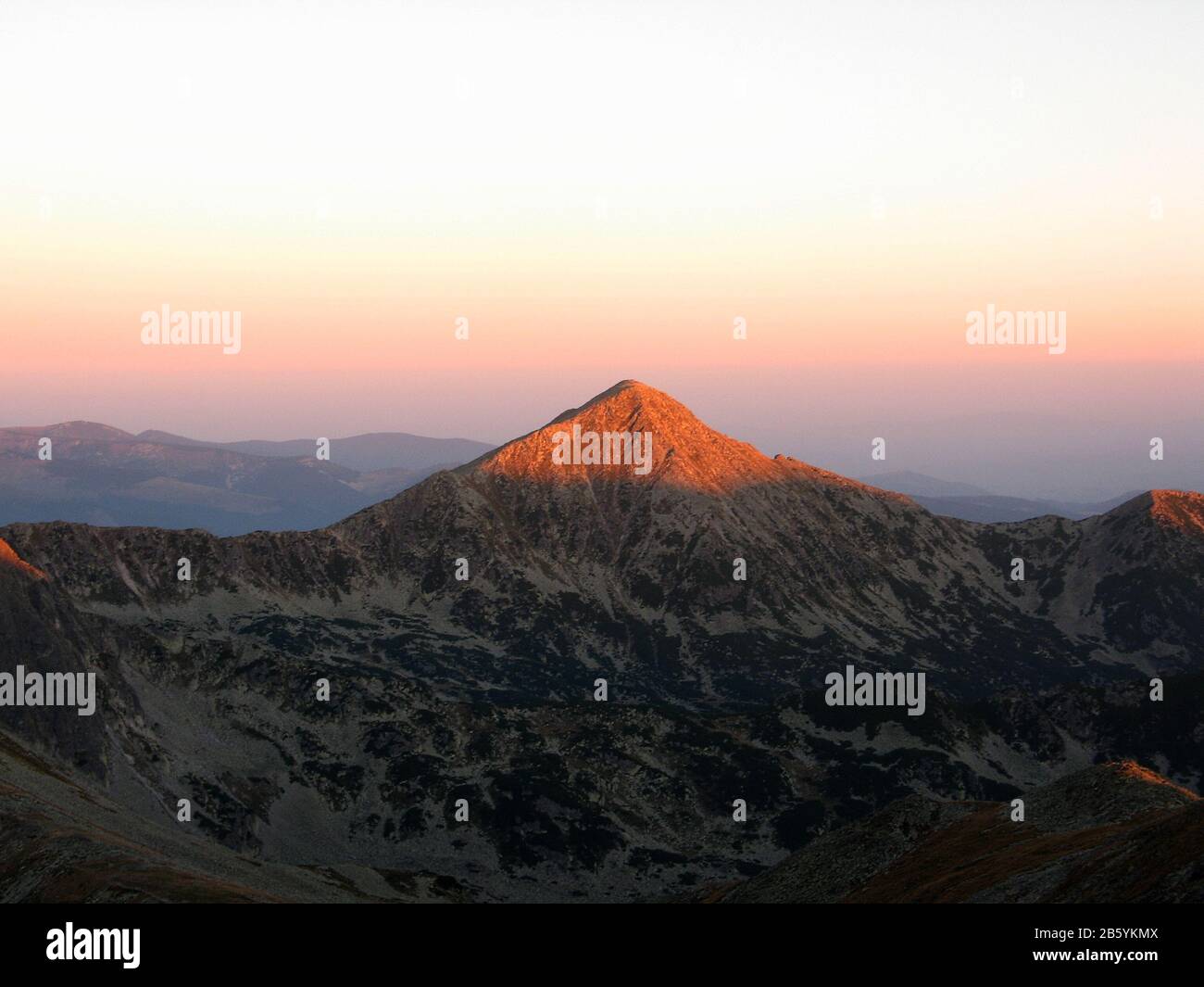 Sunrise over a pyramid-shaped mountain peak during late summer in the ...