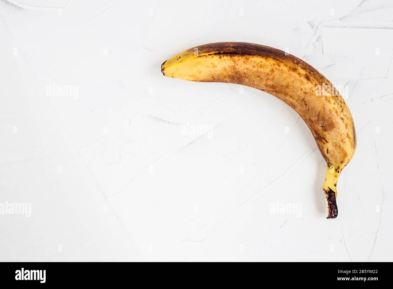 Old brownish-brown darkened banana in a skin. Ugly food. Dark banana ...