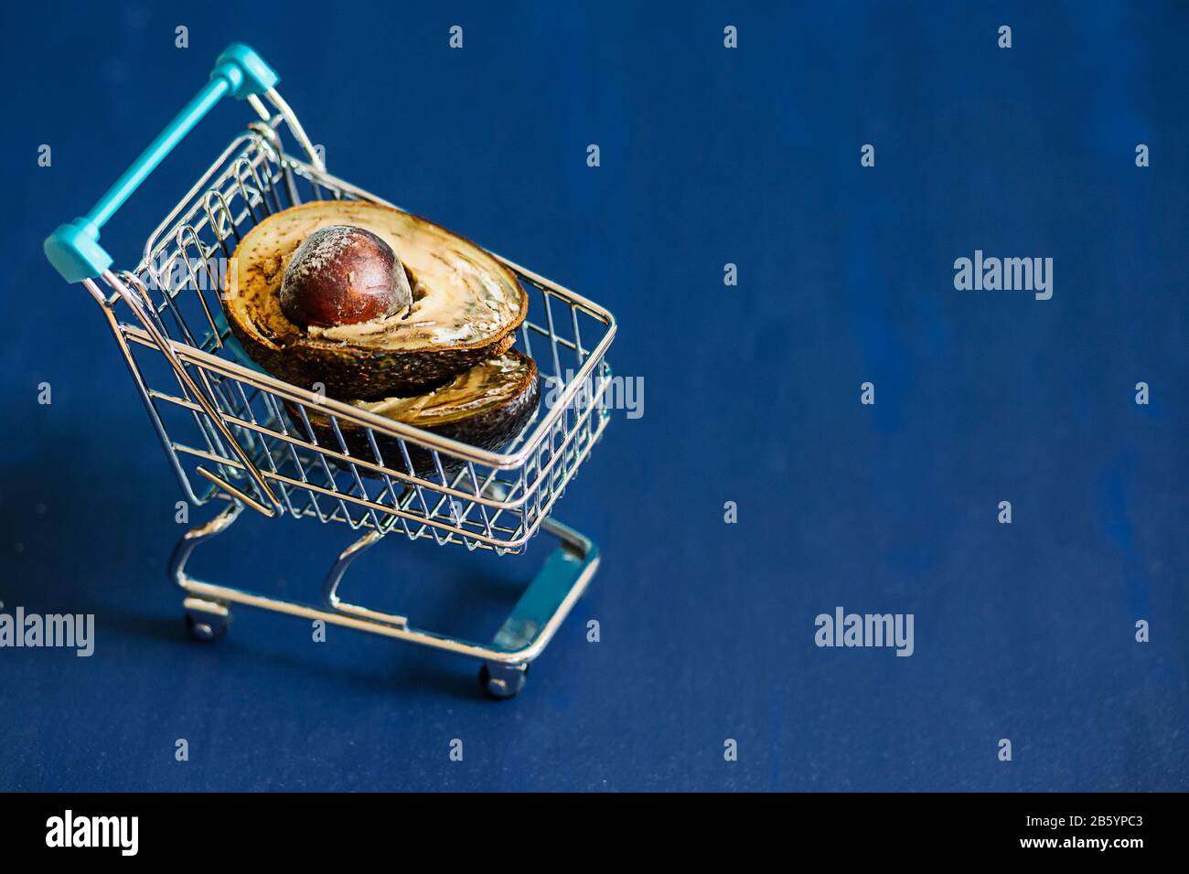 Spoiled and rotten avocado with mold in a mini food cart on a blue ...