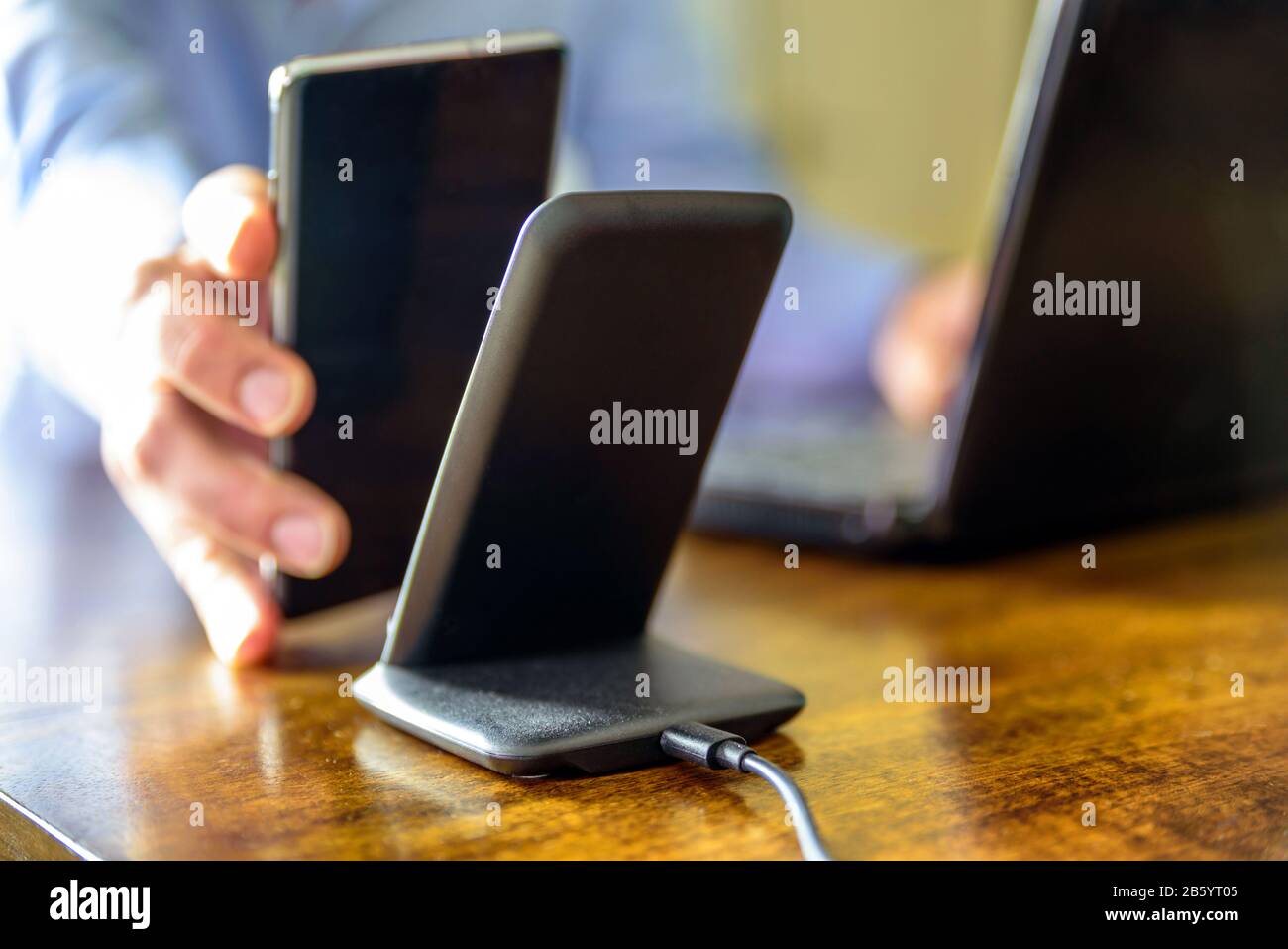 man charging smartphone using Wireless charging stand at home office ...