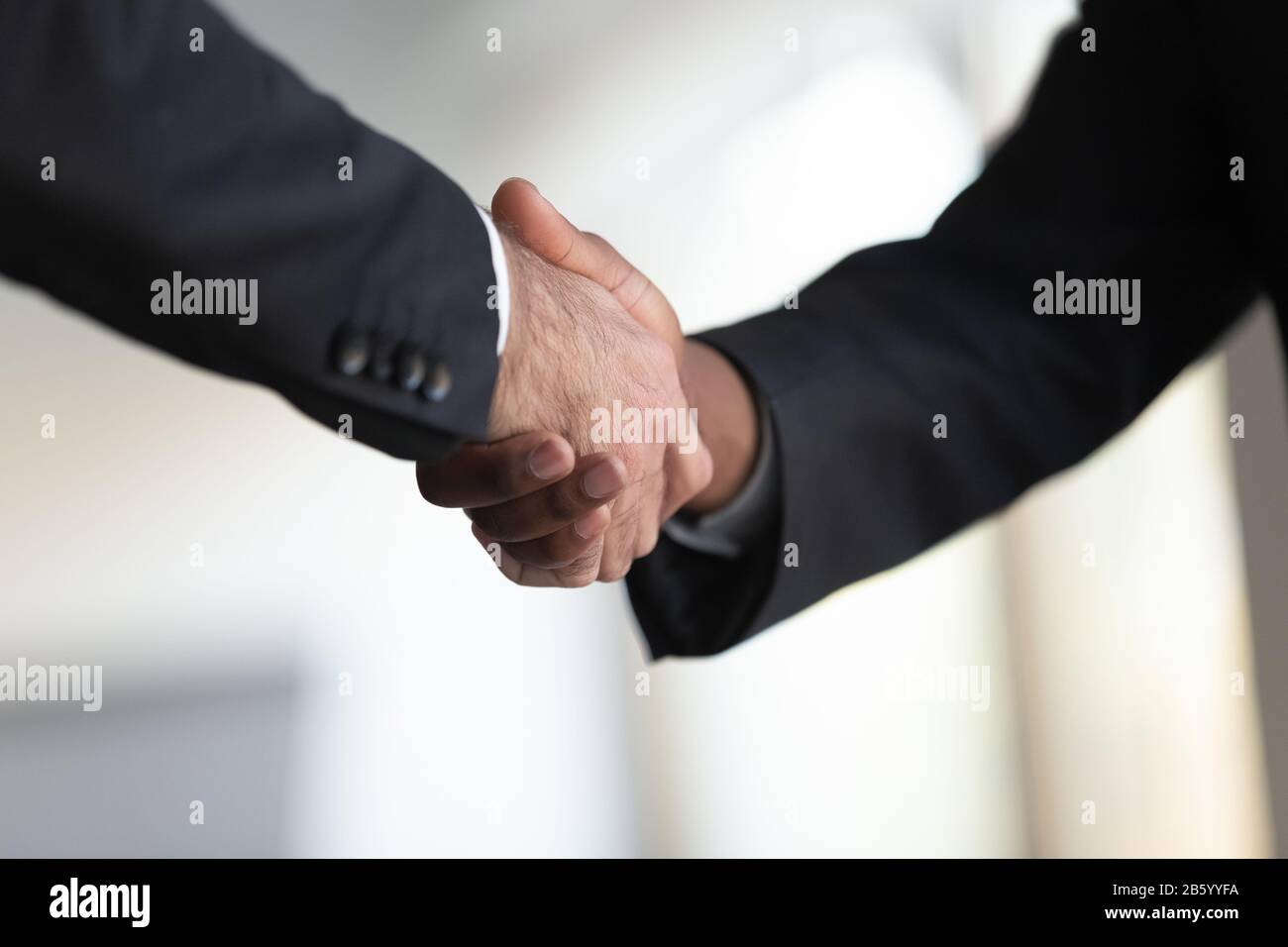 Two mixed race businessmen in suits shaking hands at office Stock Photo ...