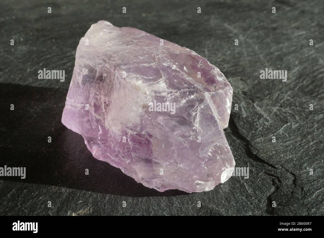 Uncut and raw amethyst chunk on gray slate background, lit by the sun ...