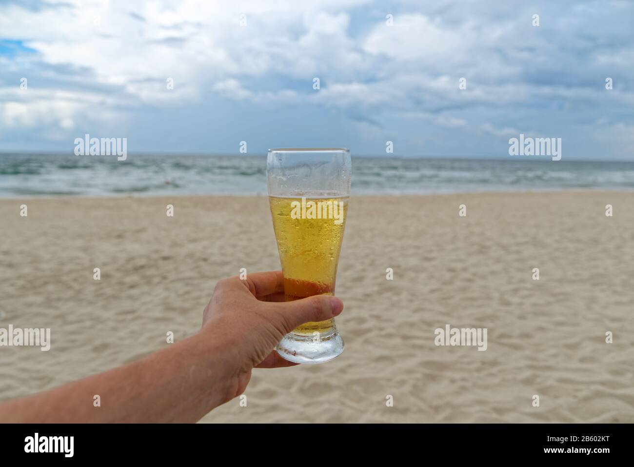 Male hand holding glass of beer on the beach against cloudy sky Stock ...