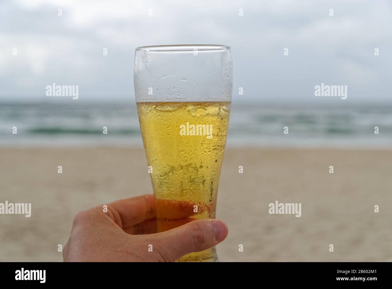 Male hand holding glass of beer on the beach against cloudy sky Stock ...