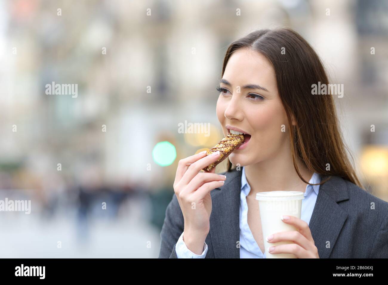 Portrait of a satisfied business woman eating a cereal snack bar ...