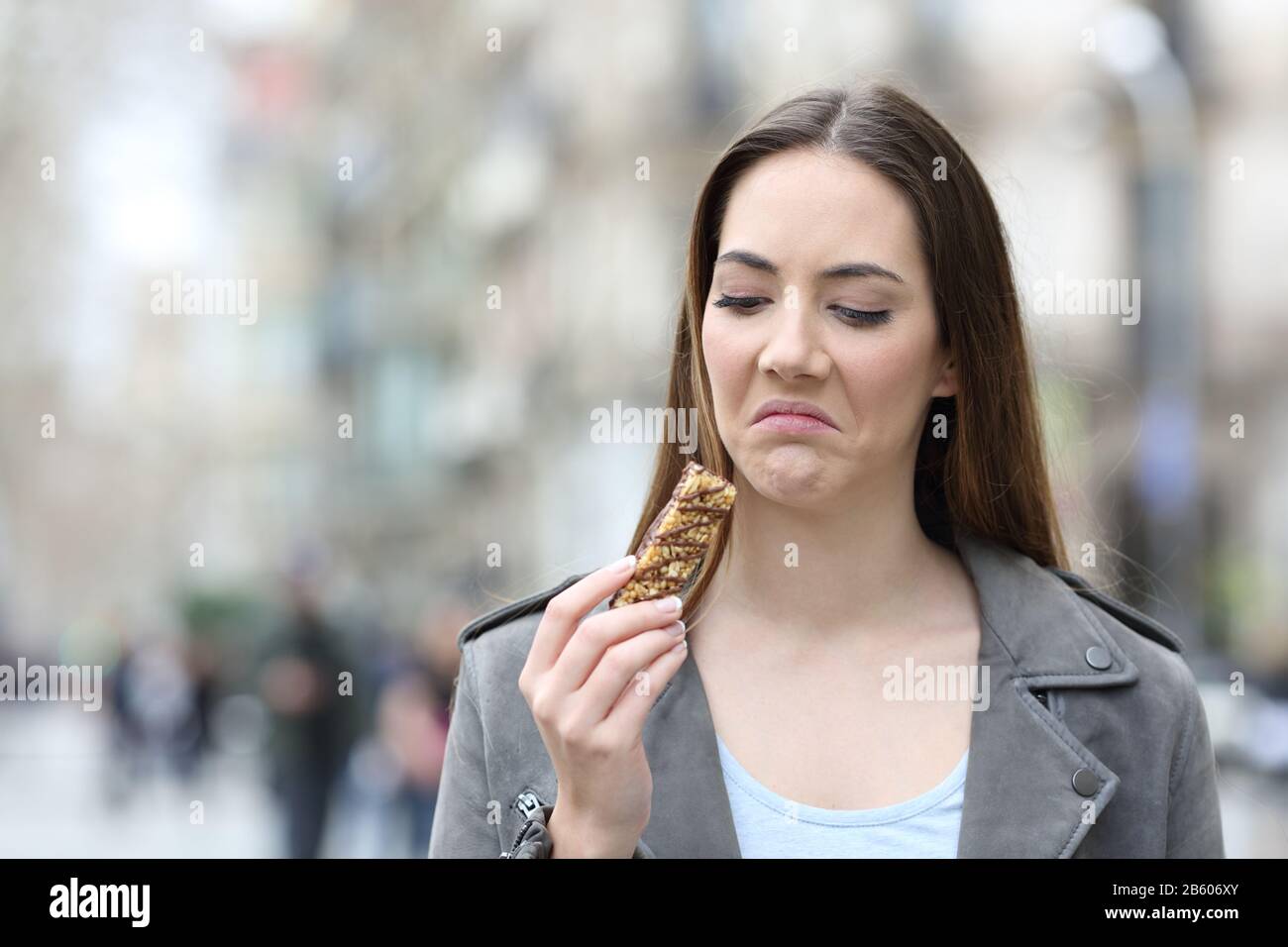 Front view portrait of a disgusted woman looking at snack cereal bar on ...