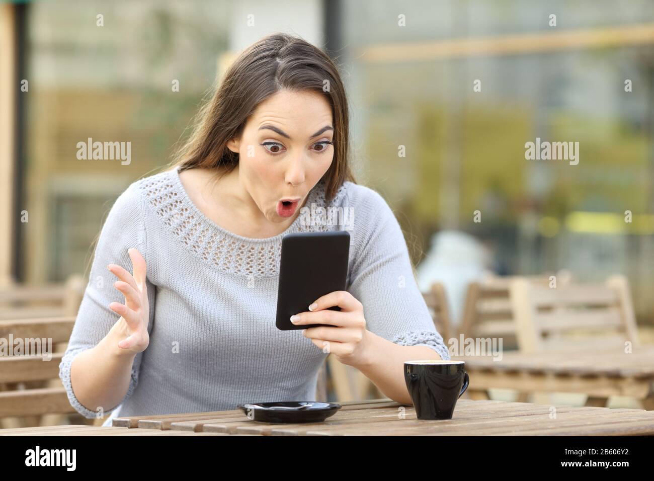 Amazed girl looking surprised at her smart phone on a cafe terrace ...
