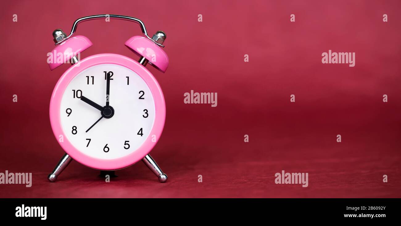 Save time, daylight saving concept, pink alarm clock on a red ...