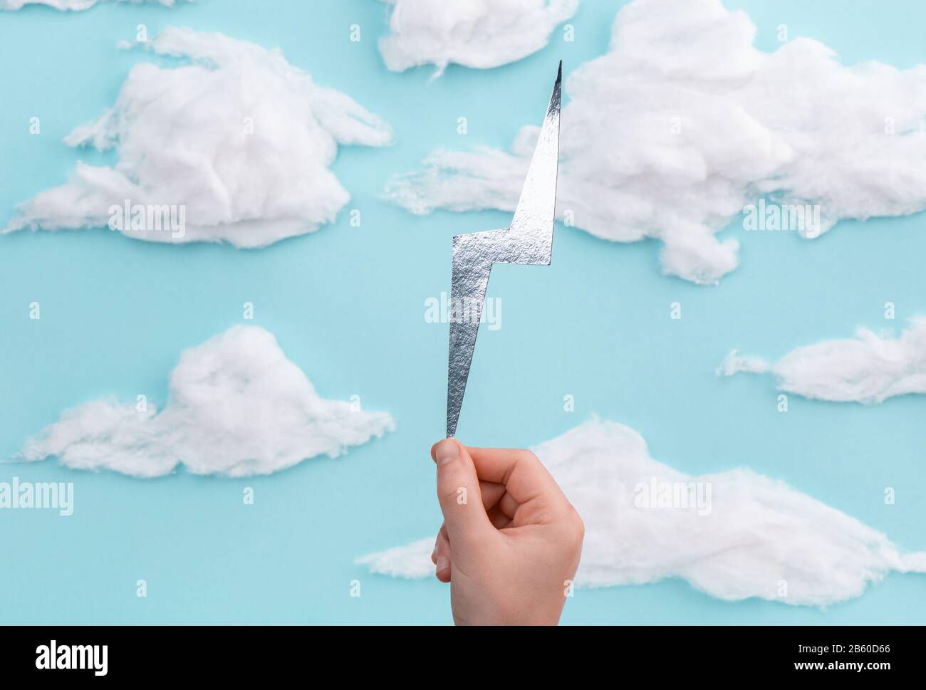 Silver lightning figure in child's hands on hand-crafted blue sky ...