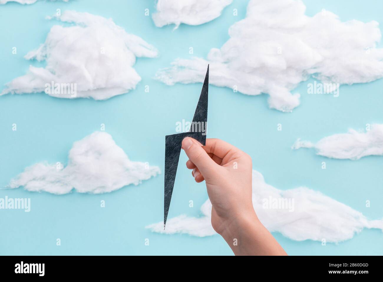 Child's hand holding a cut-out lightning on handmade blue background ...