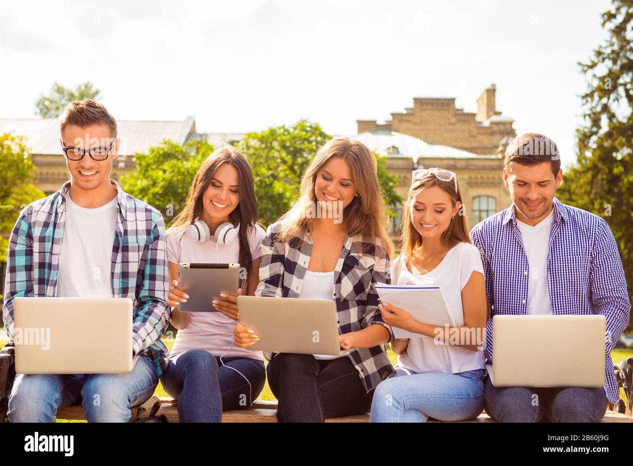 five happy smiling diverse students sitting on bench and study up with ...