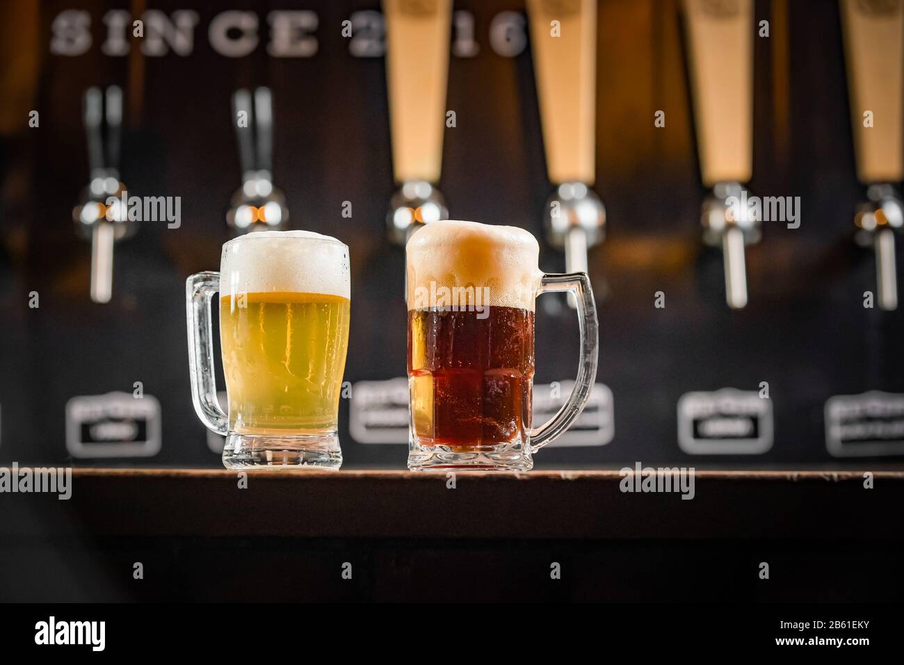 Two mugs full of chopp, one with pilsen chopp and one with dark chop on ...