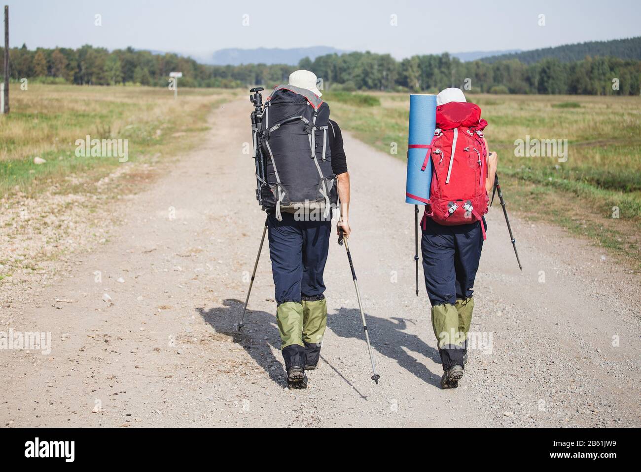 Back view of couple hikers with backpacks walking along an empry rural ...
