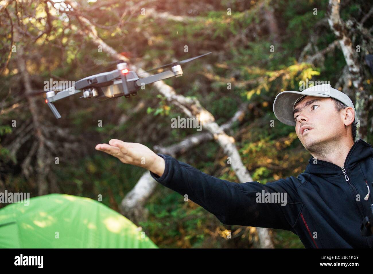 A man in a camping on the background of a tent launches a flying drone ...