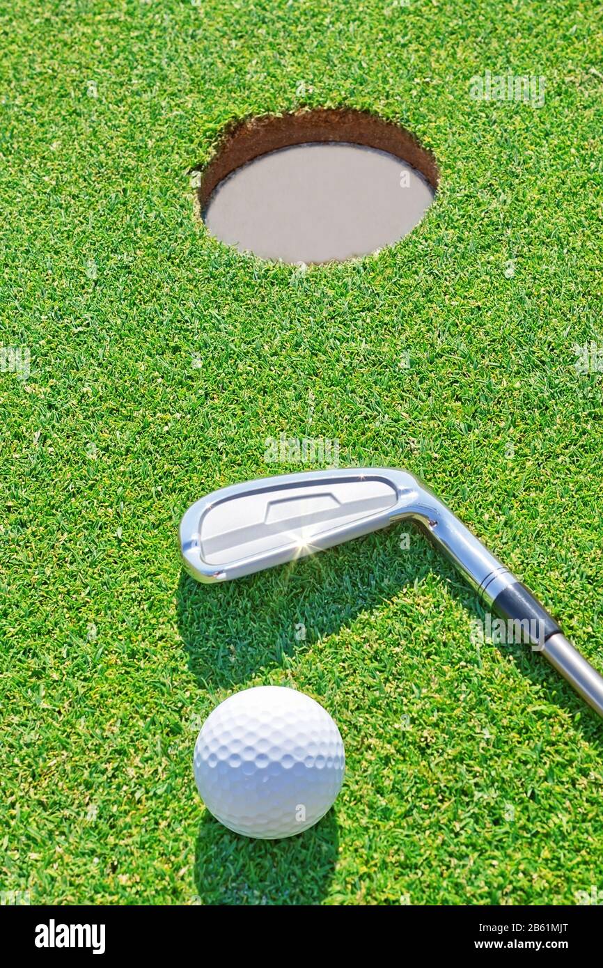Golf putter ball near the hole in the vertical format. Against the ...
