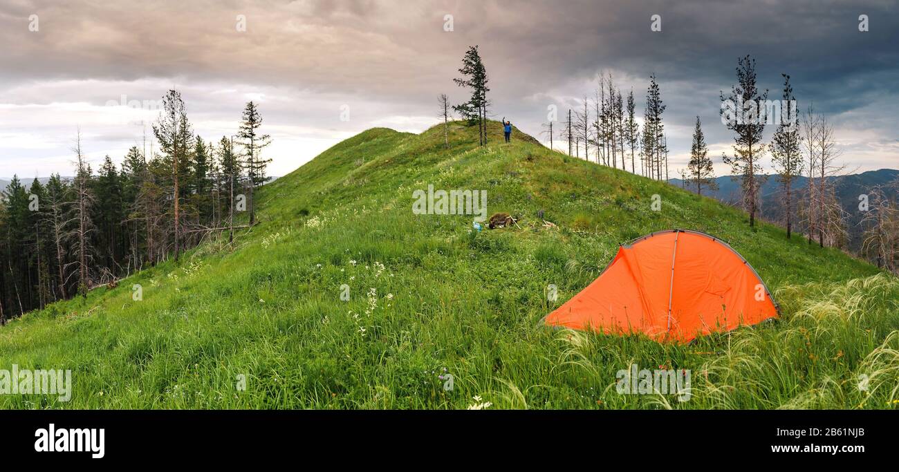 Orange hiking tent on the top of the hill beneath fresh grass, summer ...