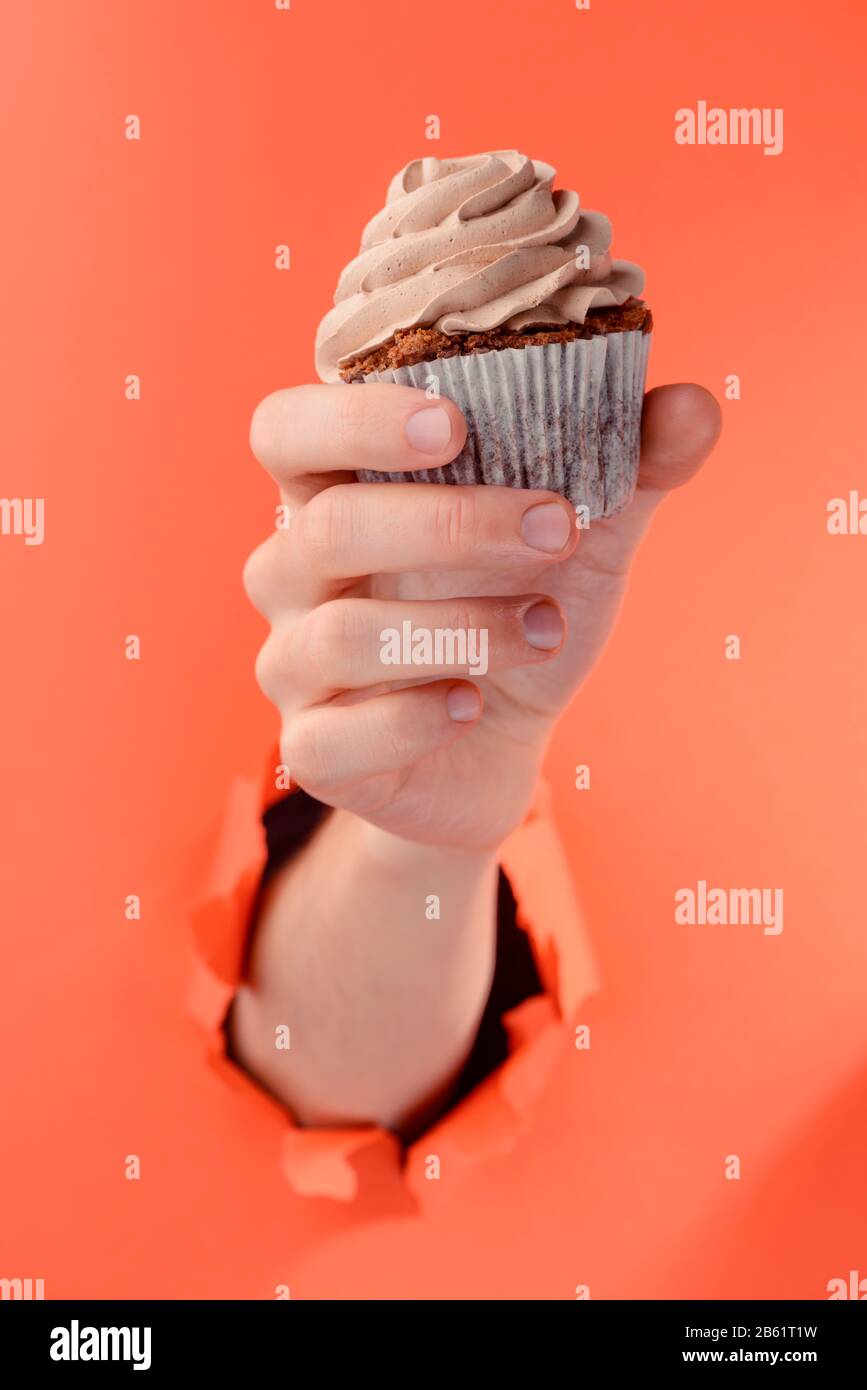 Hand giving a cupcake through a torn hole in red paper background Stock ...