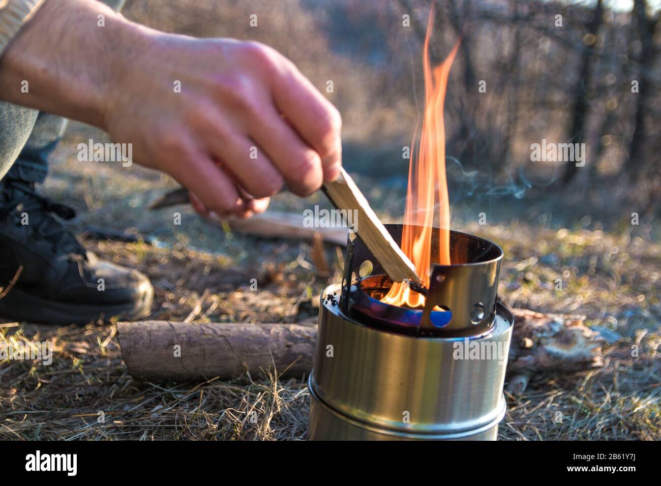 closeup man hands sets fire with straws a in a portable wood burner in ...
