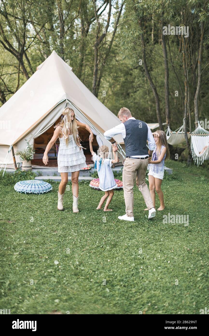 Dancing together, outdoors, camping, picnic with wigwam. Happy family ...