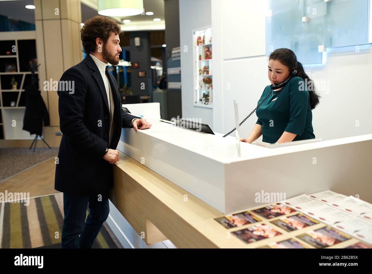 female receptionist helping man to choose a room, woman making a phone ...